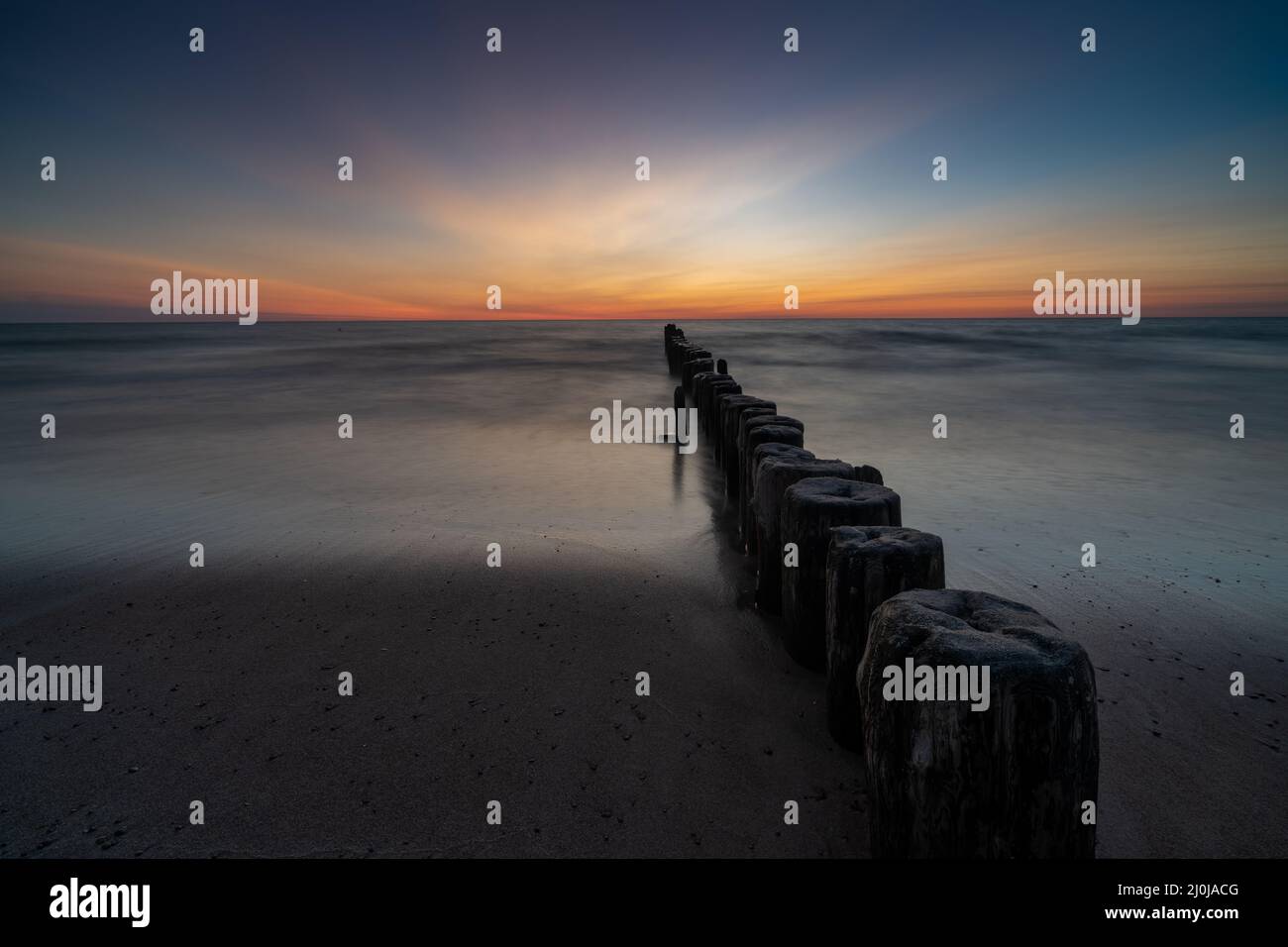 Long exposure of an ocean sunset with sandy beach and wooden pylon ...