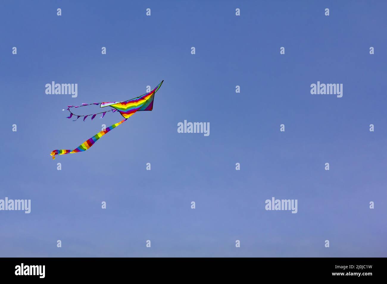 A kite painted in the colors of a rainbow flies against the background ...