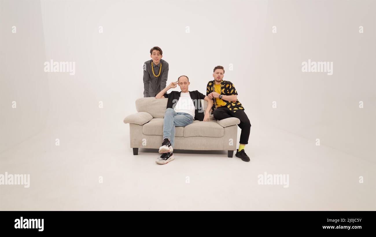 Three stylish young guys sitting on soft couch and talking on the ...