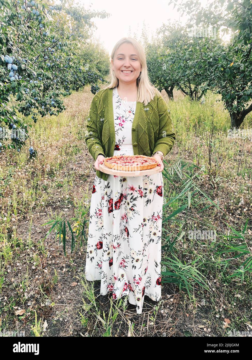 Blond happy female in dress and knitted jacket carrying board with ...