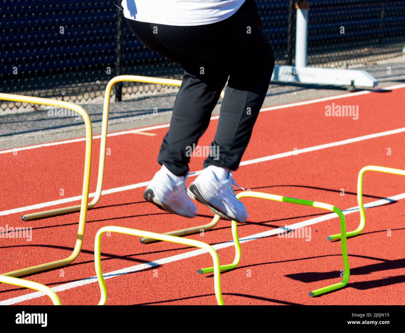 A high school boy is jumping over small yellow hurdles on a red track ...