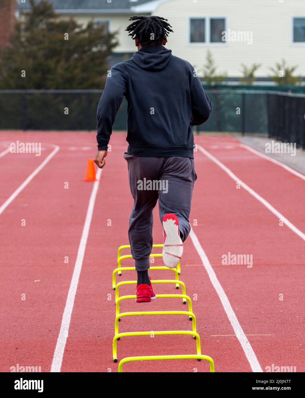 Rear view of an African American track runner is running over yellow mini banana hurdles in a ...