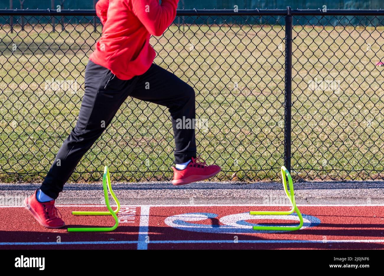 A high school boy is standing over a yellow mini hurdle in the A ...