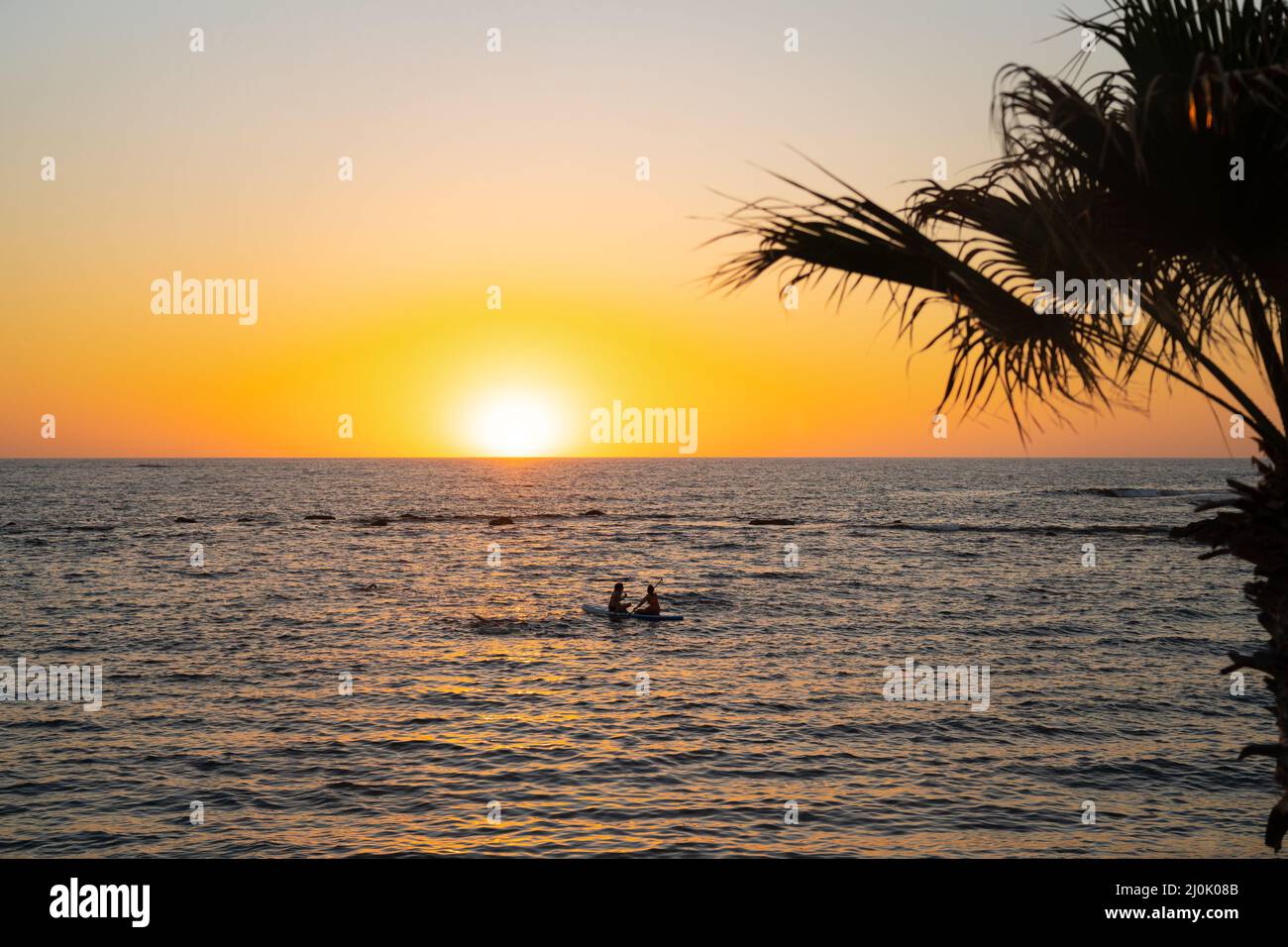 Two women sharing paddle board at sunset on calm waters in ...