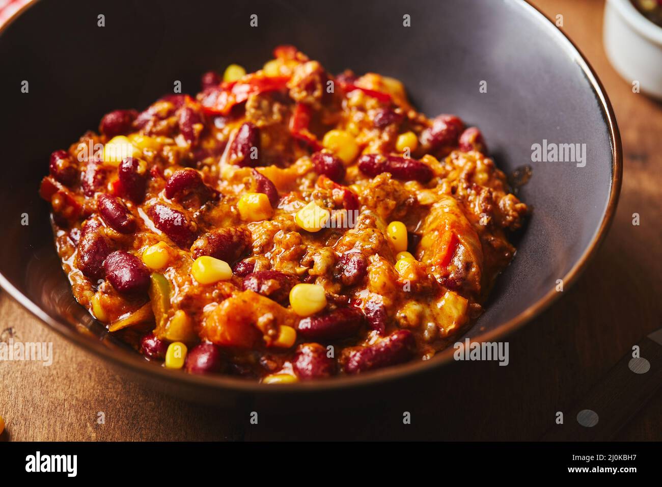 Chili Con Carne with ground beef, beans and corn in dark bowl on wooden ...