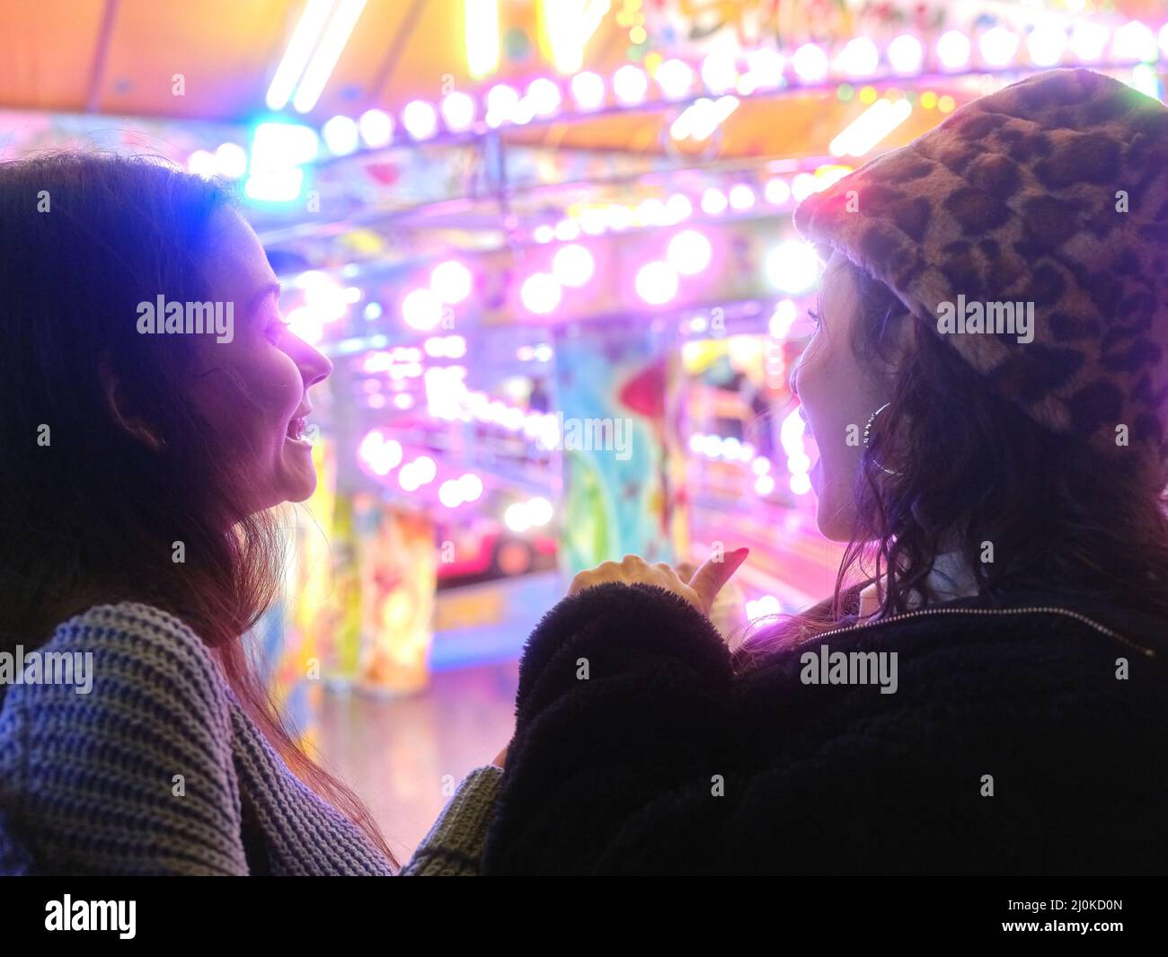 Two women talking in front of an attraction of a colorful evening fair ...