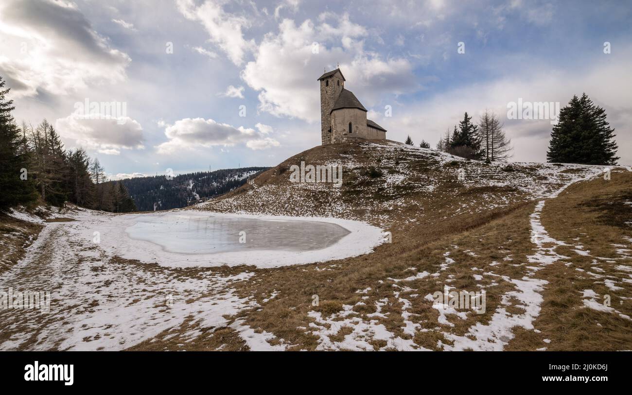 Small ancient church on the top of a small snowy hill in winter under a ...