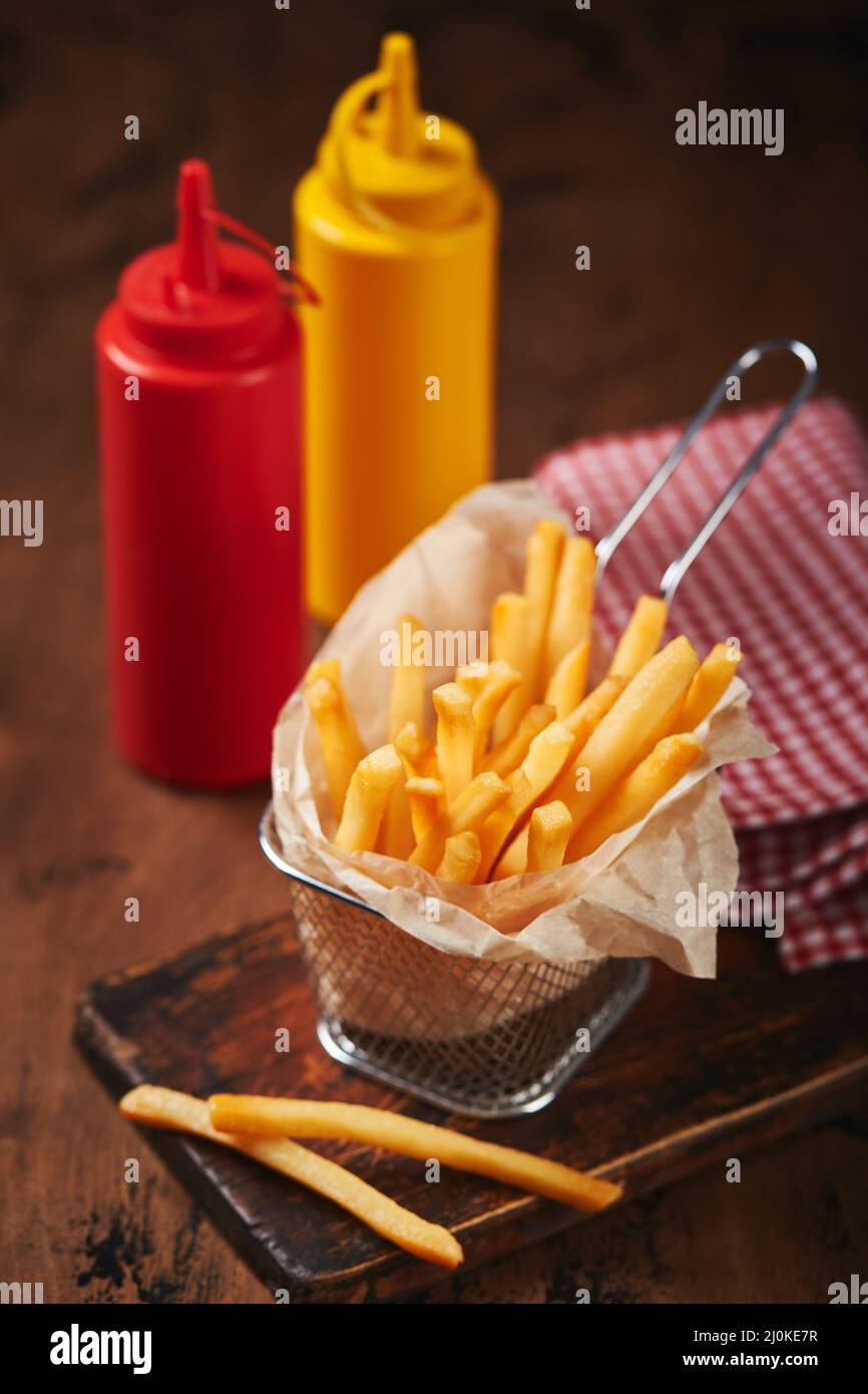 French fries in a metal mesh basket on a wooden board. Fast food ...