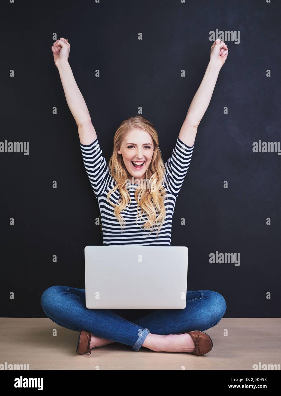 Success feels great. Portrait of a young woman using a laptop against a ...