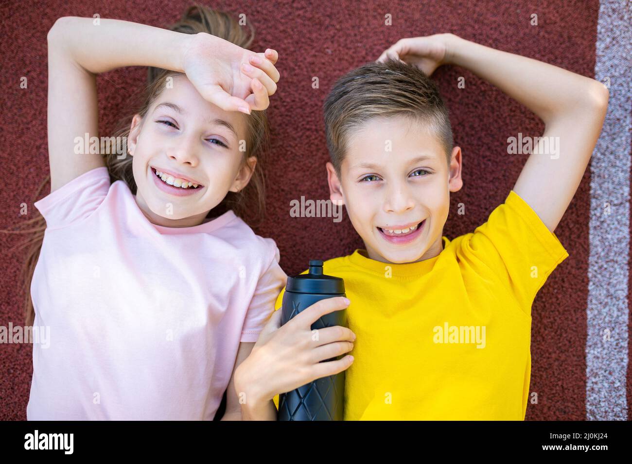 Happy sports kids brother and sister twins lie on running track at ...