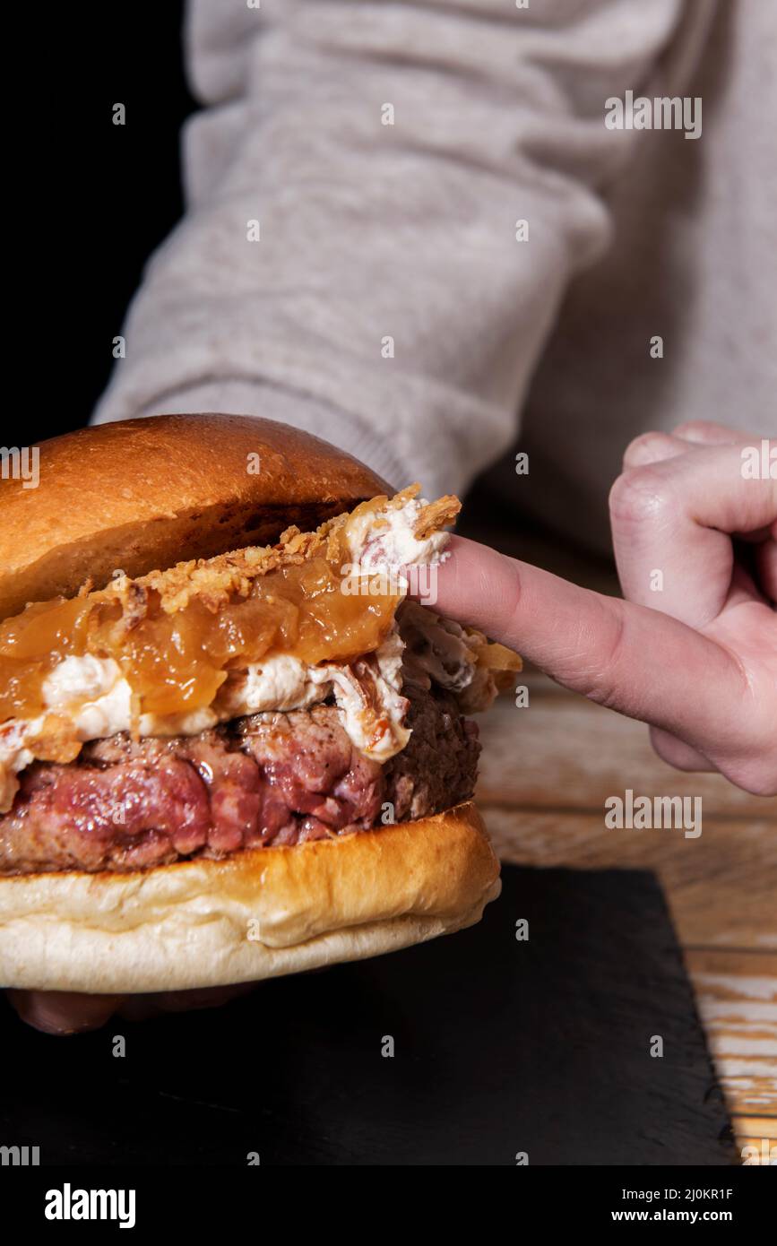 Holding in two hands an amazing beef burger with a lot of cream cheese ...