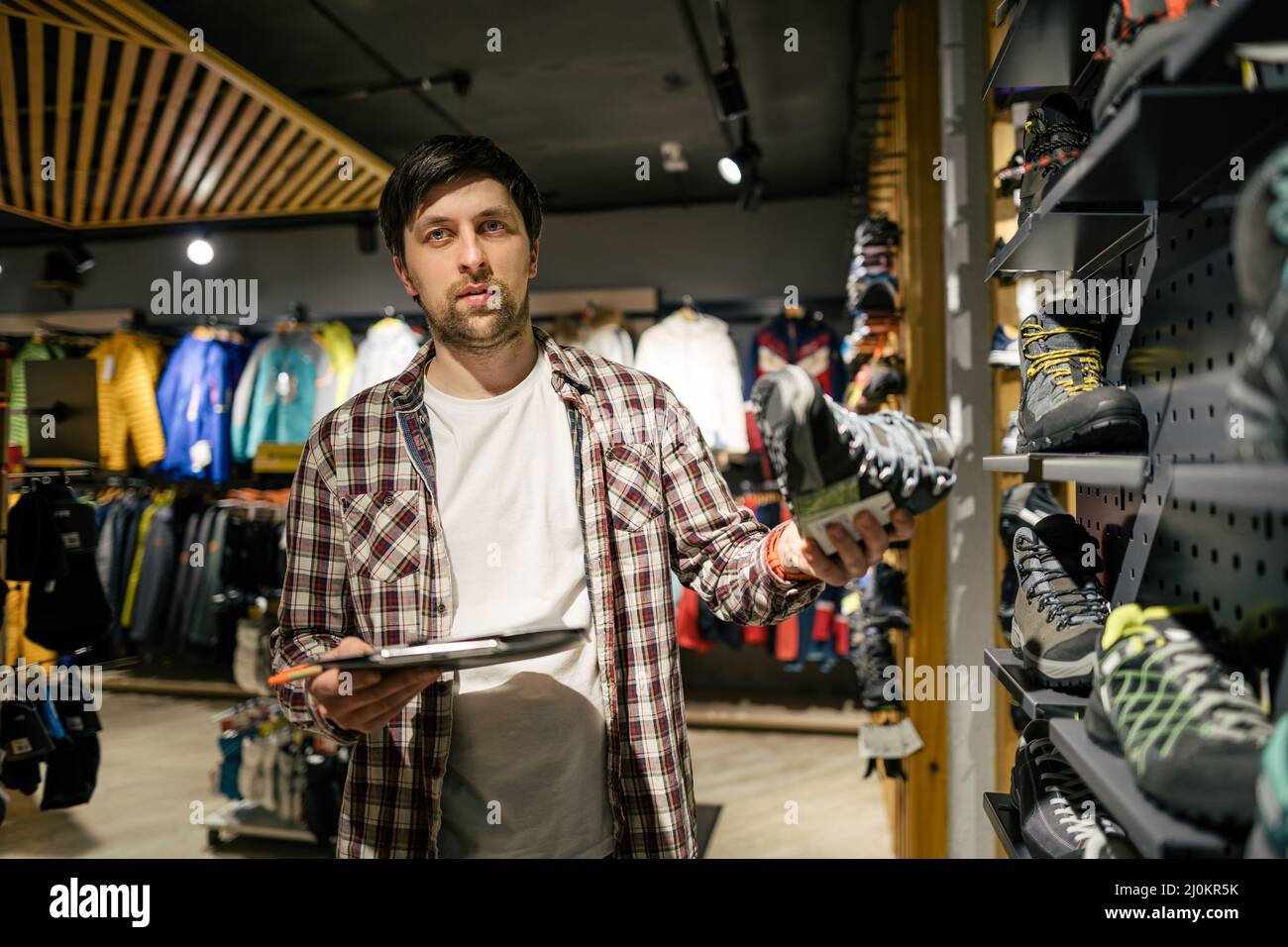 Store clerk helping customer try hiking boots at outdoors equipment ...