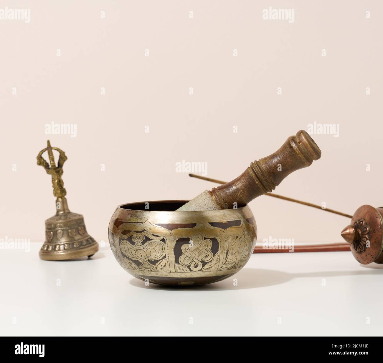 Copper singing bowl and wooden clapper on a white table. Musical ...