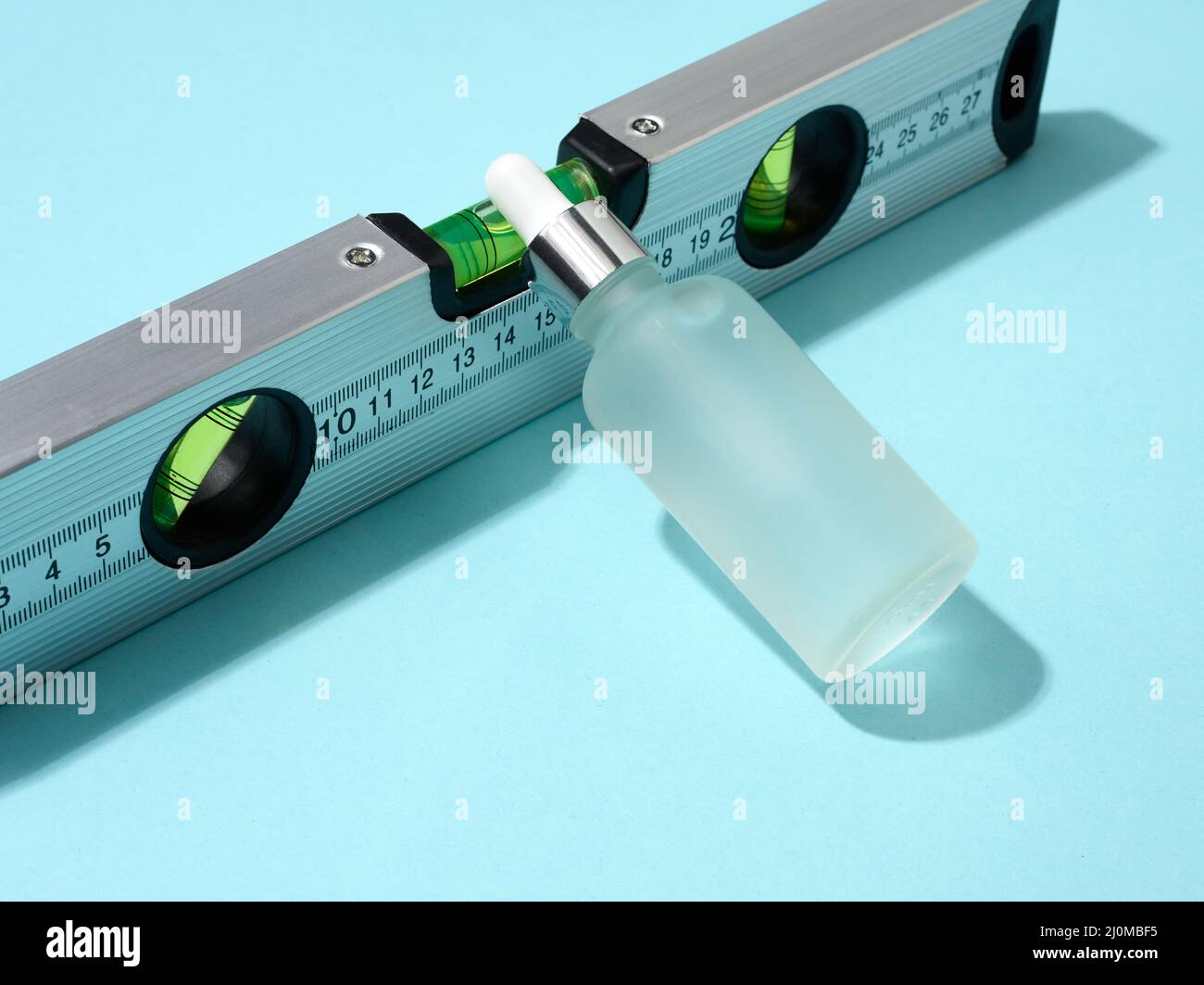 White glass bottle with a pipette lies on a building level on a blue ...
