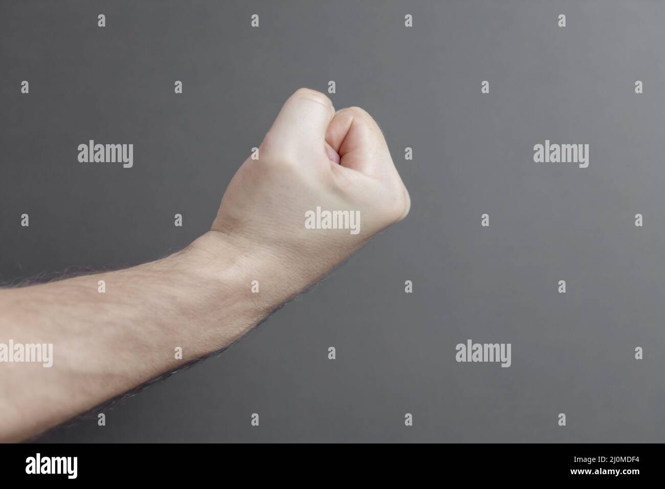Male hand clenching a fist on a light gray background, close-up. Copy ...