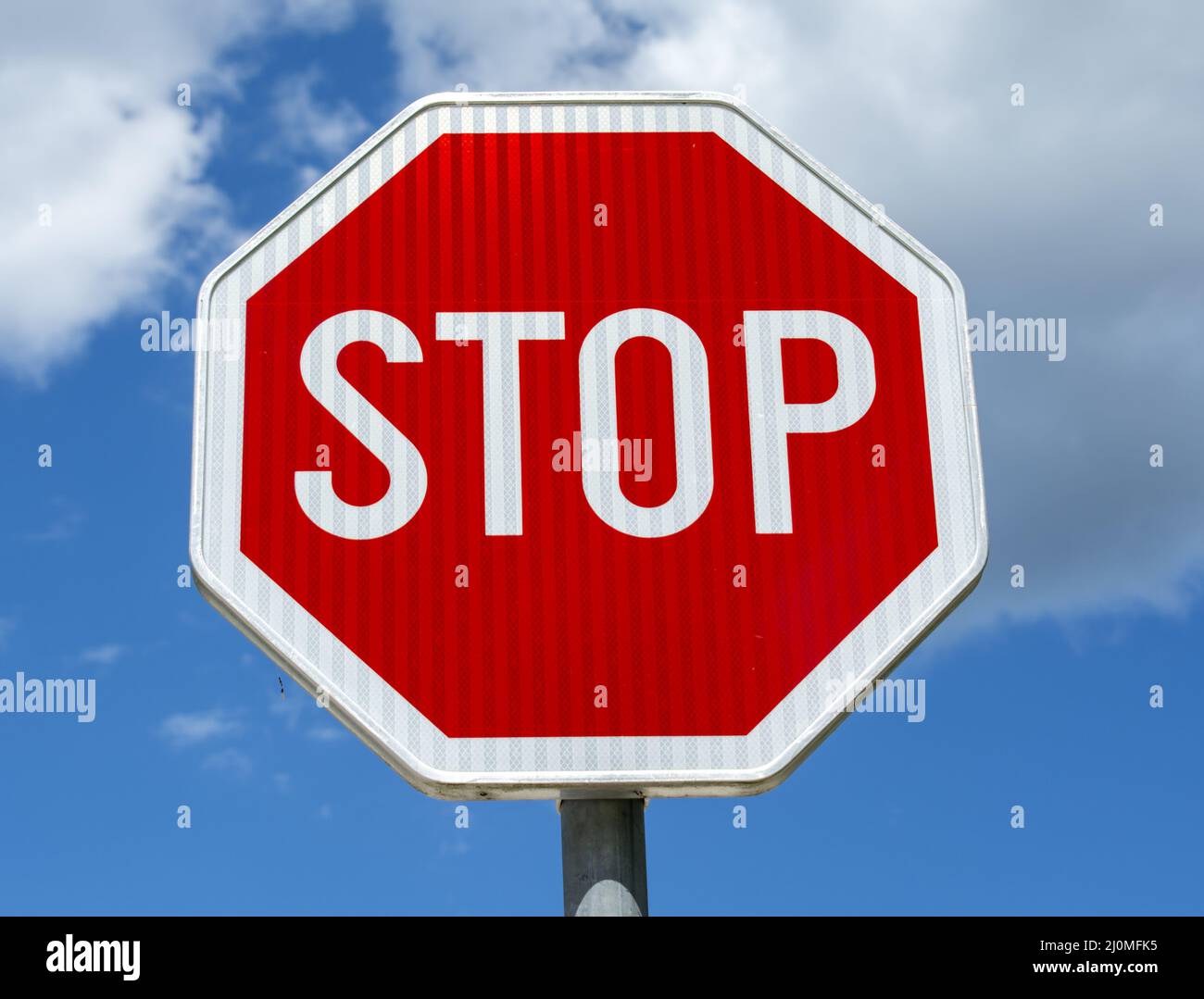 Red octagonal Stop sign on a metal pole with cloudy sky in the ...