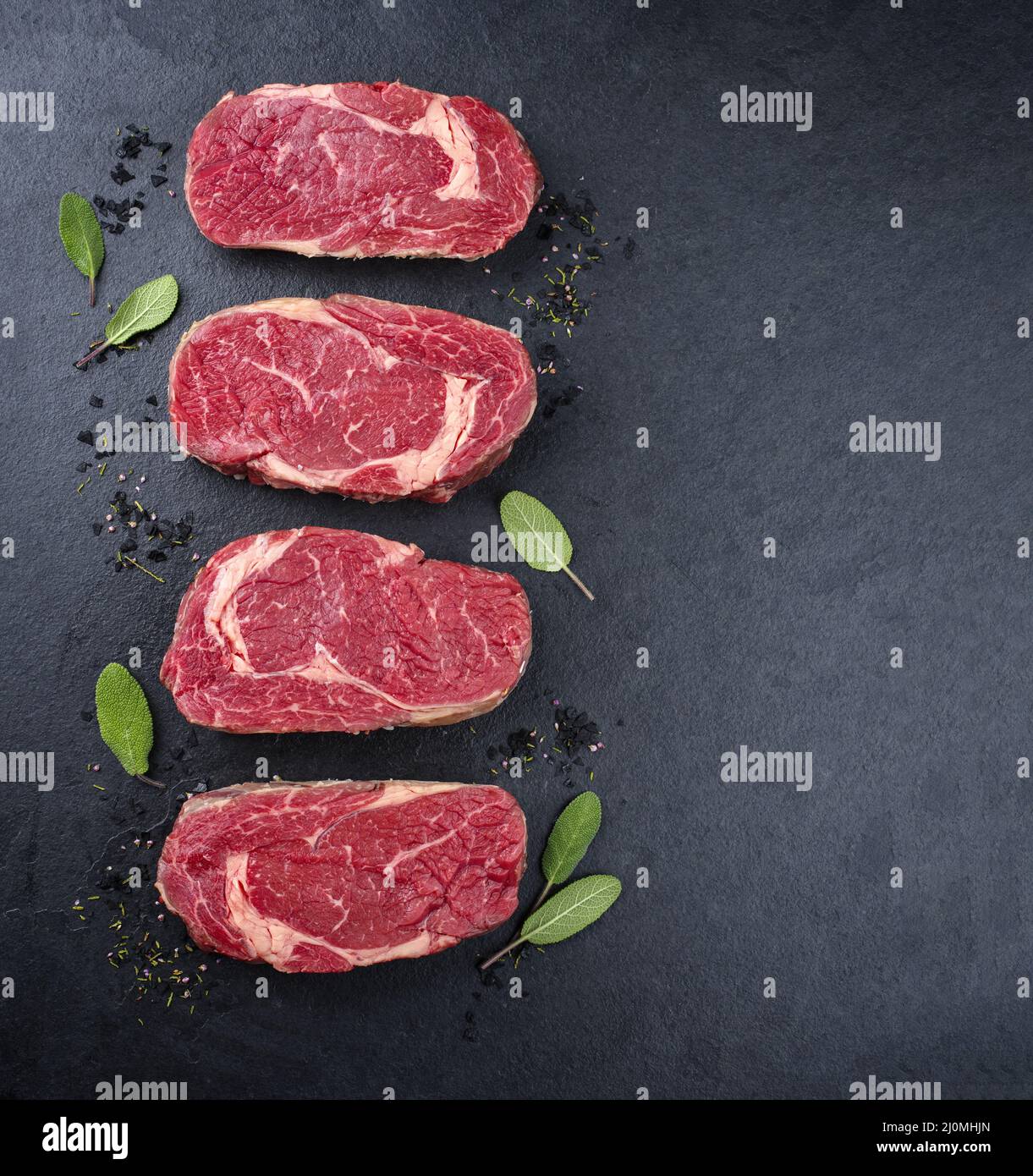 Four raw dry aged wagyu rib-eye beef steaks with herb and black salt ...