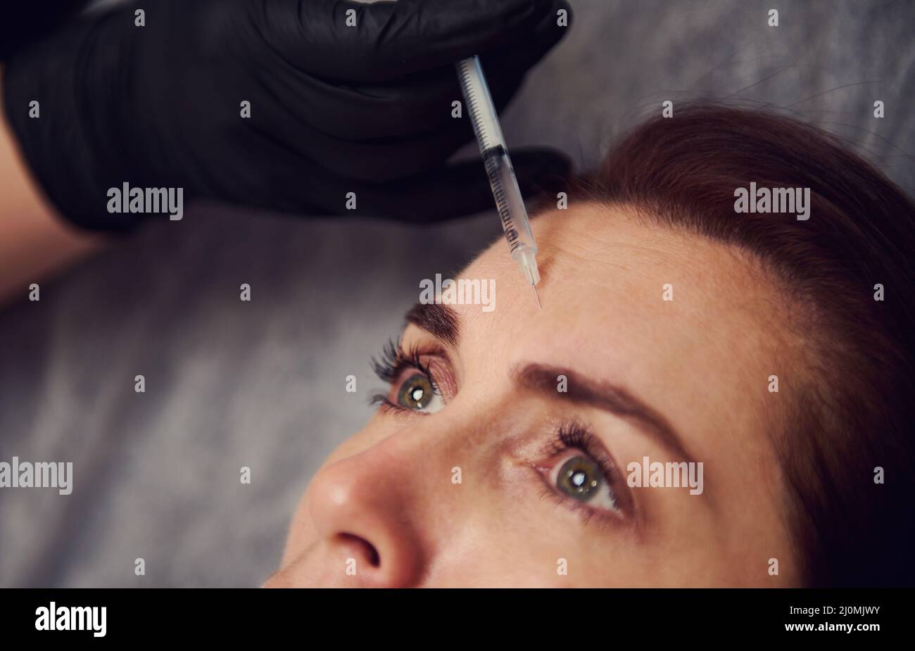Close-up of cosmetologist making injection in the forehead of a woman ...
