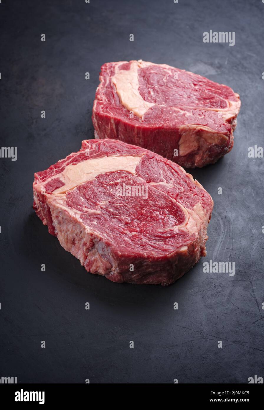 Raw dry aged wagyu rib-eye beef steaks offered as close-up on a rustic ...
