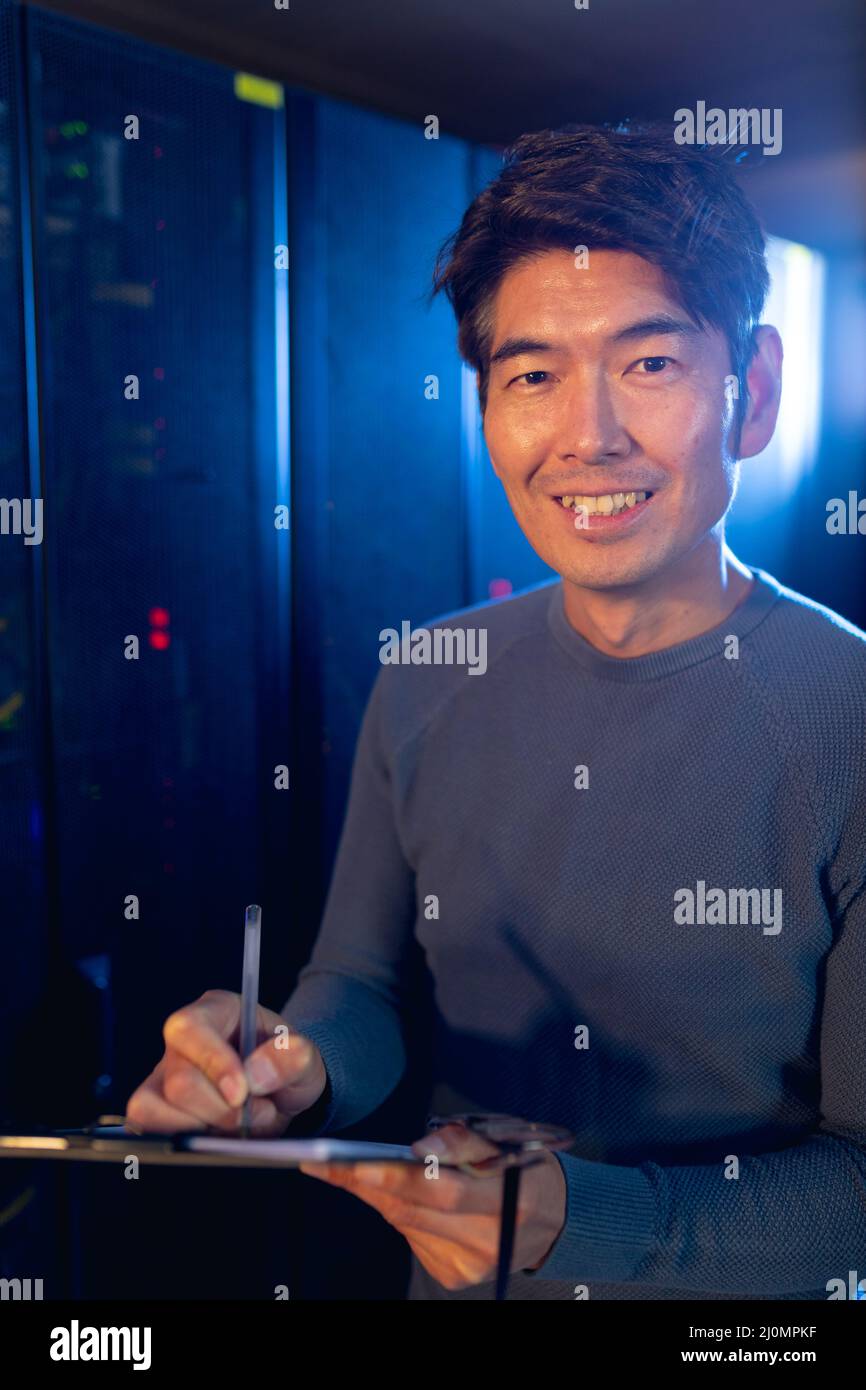 Portrait of asian male engineer smiling while writing on clipboard in ...