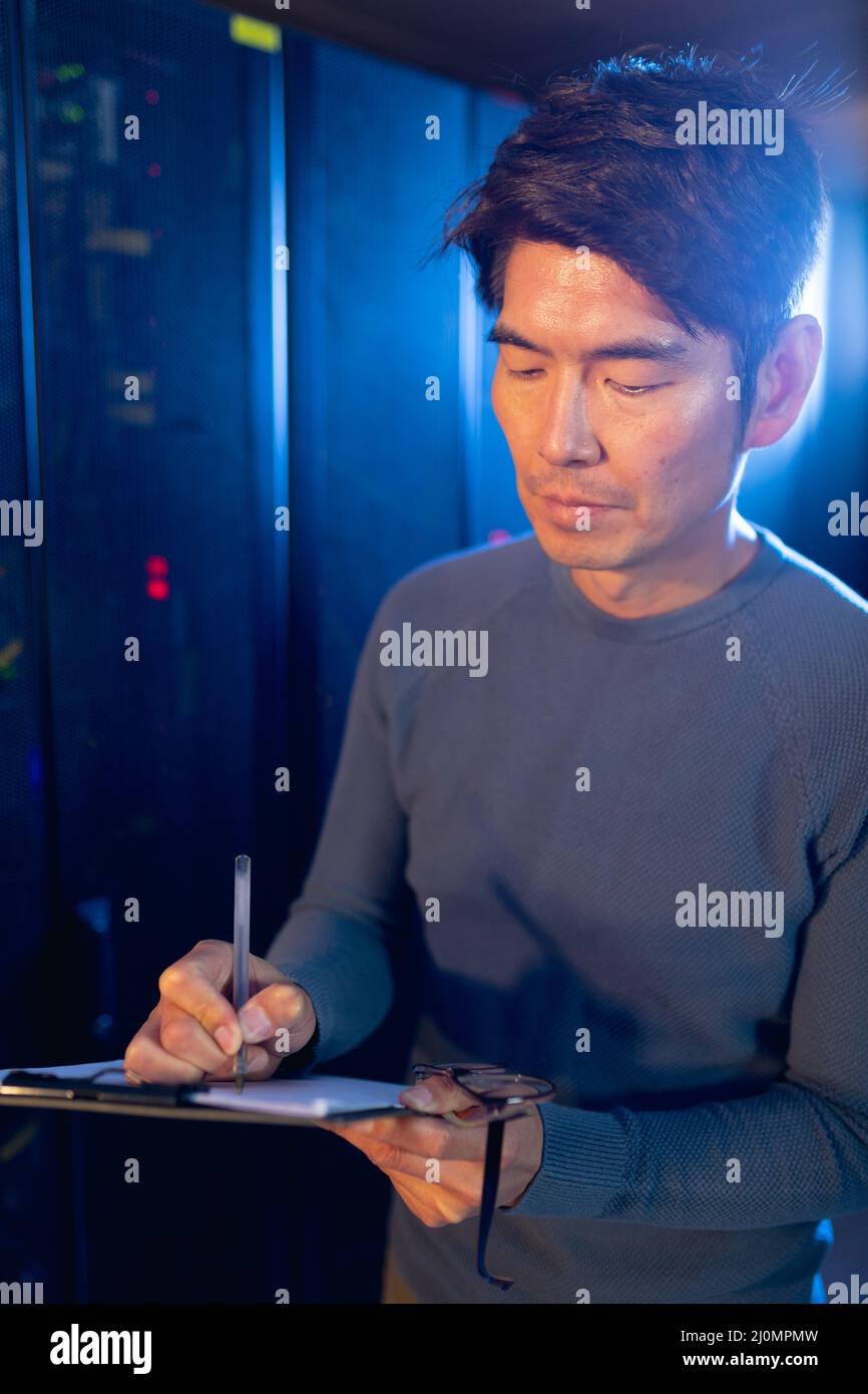 Asian male engineer writing on clipboard in computer server room Stock ...