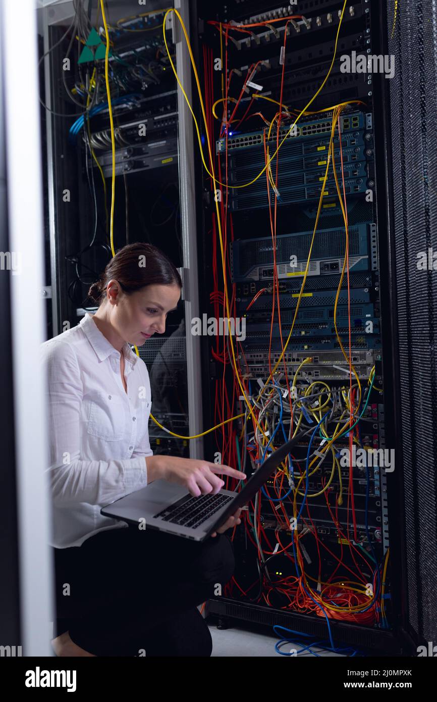 Caucasian female engineer with laptop inspecting computer server in ...