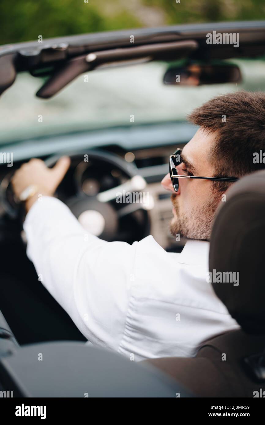 The man in white shirt sits behind the wheel of an open car, close-up ...