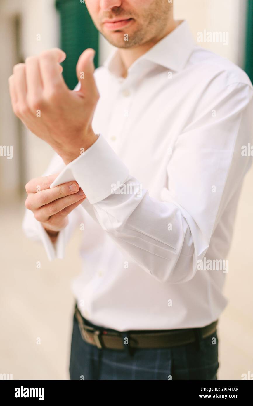 Man is buttoning the cuffs of a white shirt against the background of ...