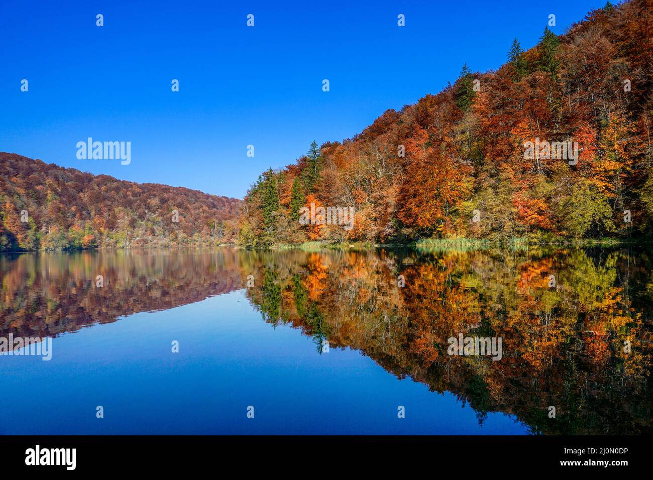 Calm blue lake with reflections of hills and forest in intense fall ...
