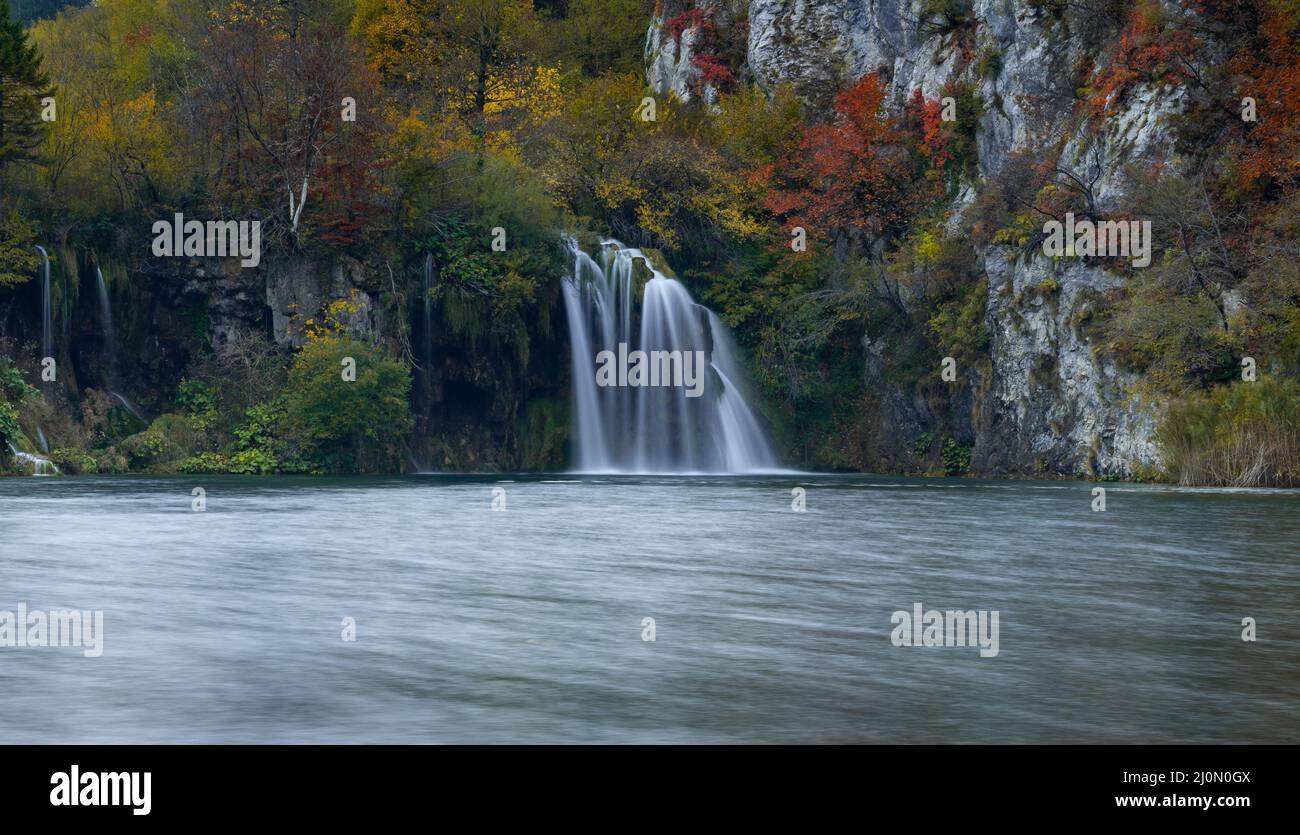 Horizontal view of calm lake with a waterfall and colorful fall foliage ...