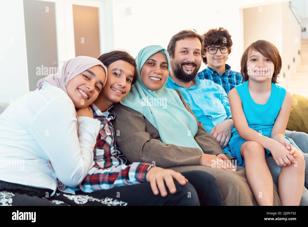 Portrait photo of an arab muslim family sitting on a couch in the living room of a large modern ...