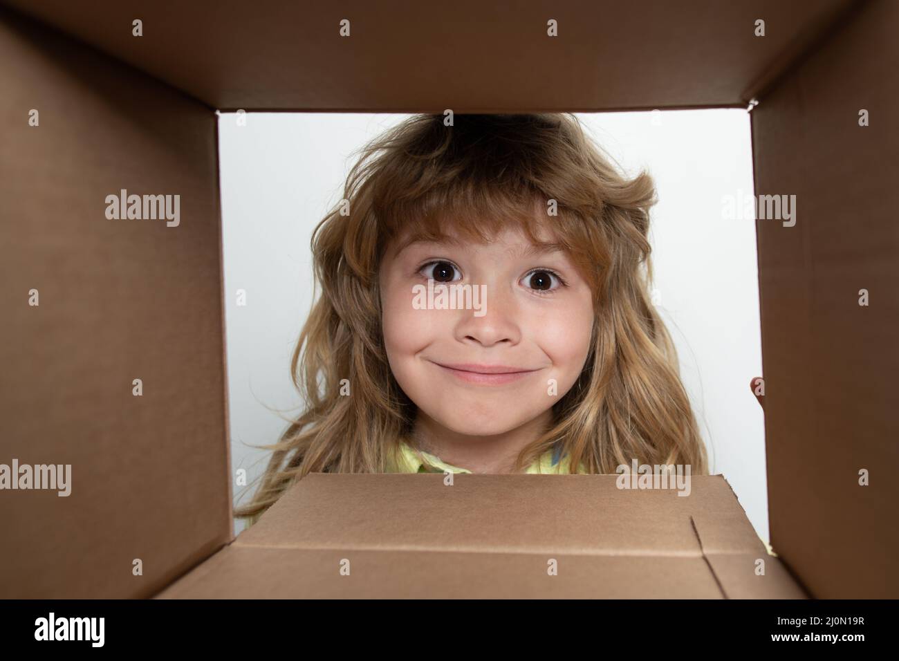 Child opens carton box and pulling out gift from it. Small boy looking ...