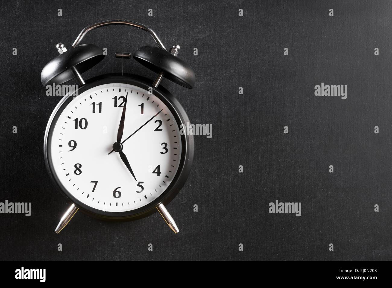 Alarm clock showing 5 o clock against black background Stock Photo - Alamy