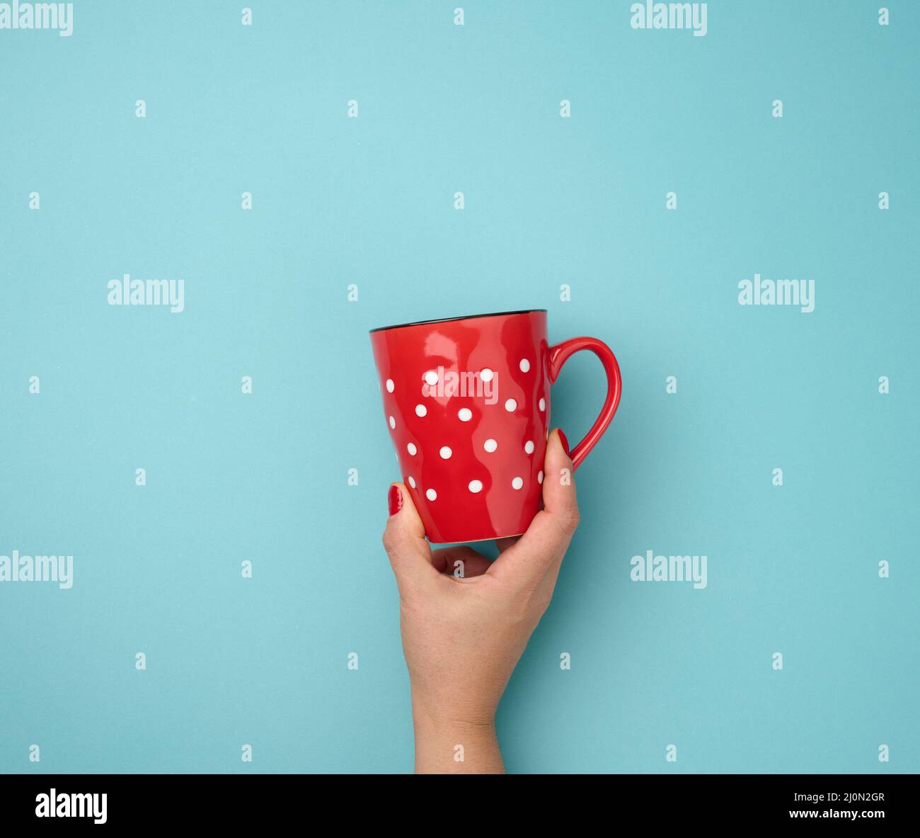 Female hand holding a red ceramic mug on a blue background, break time ...