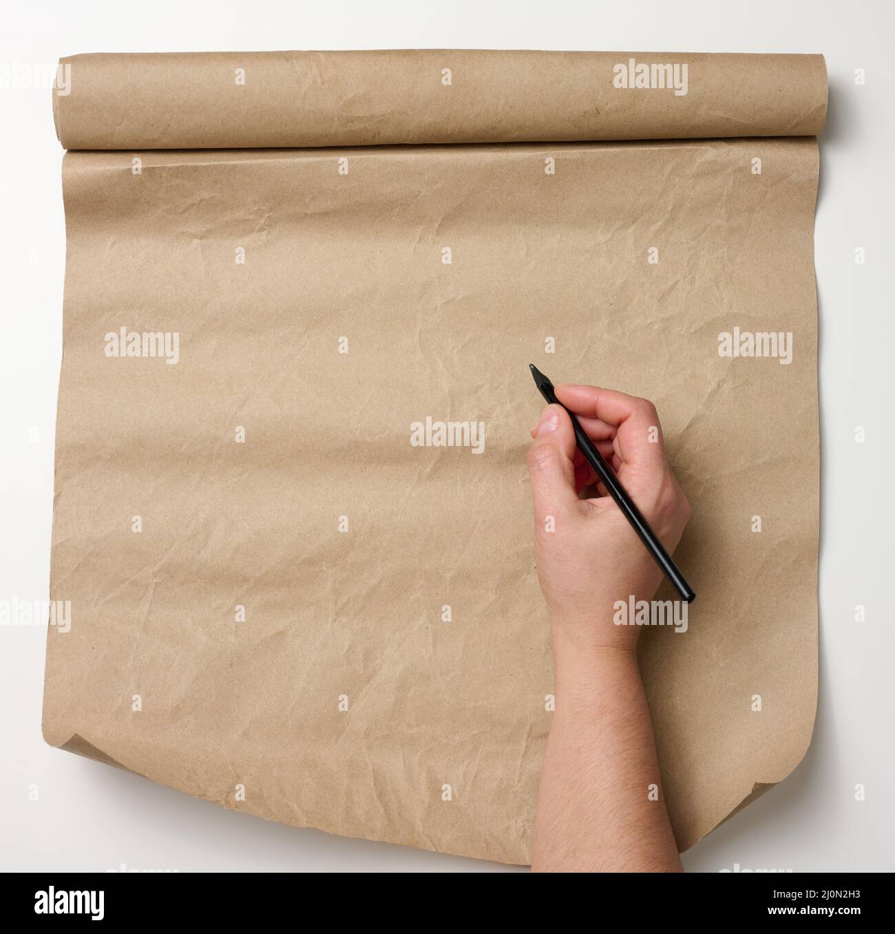 Female hand holds wooden pencil over brown paper roll on white table ...