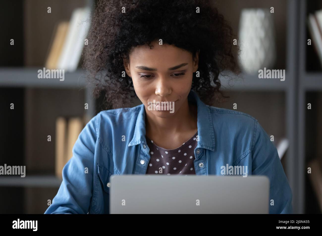Positive focused African student girl using laptop, studying in library ...