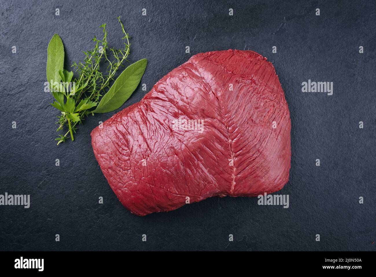 Raw dry aged bison beef rump steak piece as top view with herbs on ...