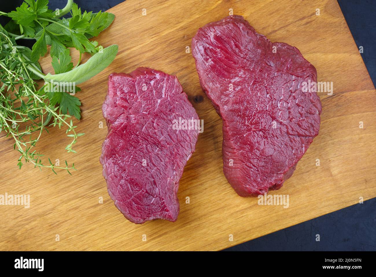 Raw dry aged bison beef rump steak piece and slices offered with herbs ...