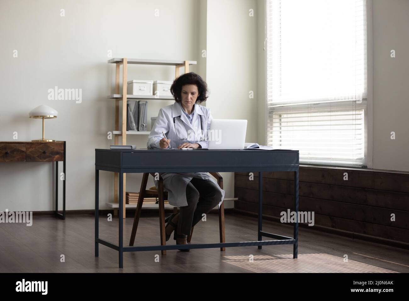 Focused serious senior head doctor working at hospital office workplace ...