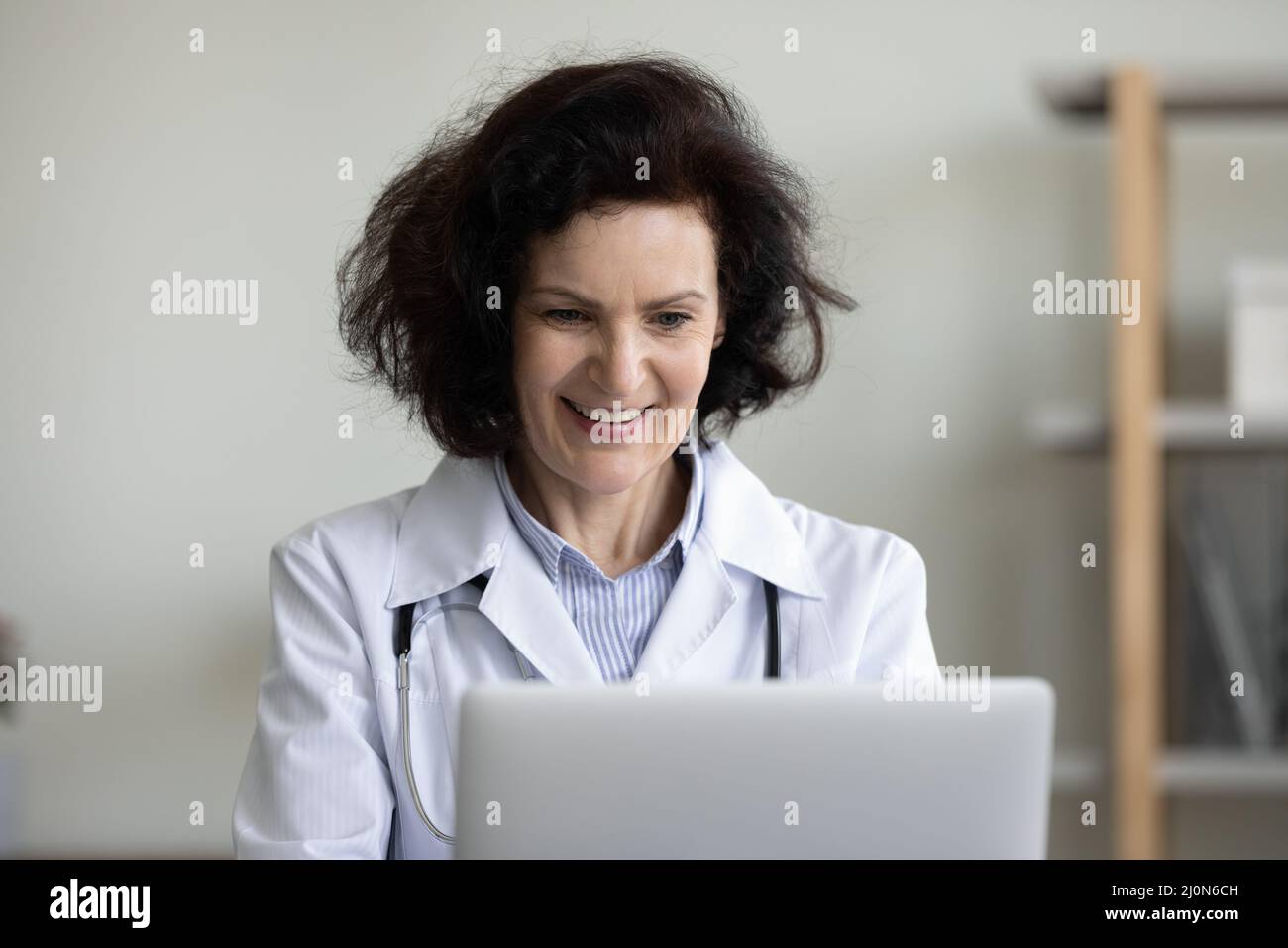 Happy mature practitioner woman using laptop in hospital office Stock ...