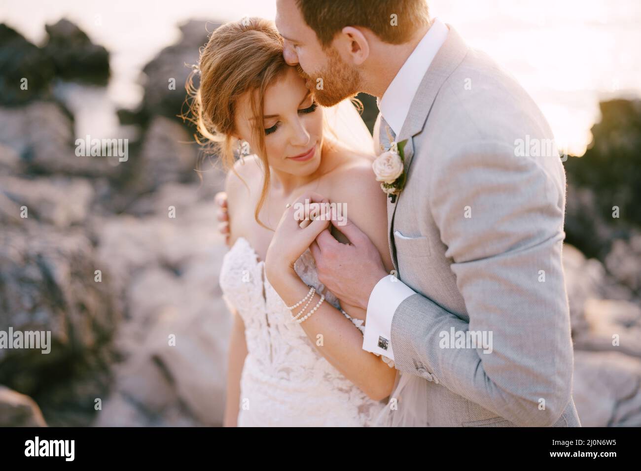 Groom kisses bride, hugging her shoulders on the rocky seashore Stock ...