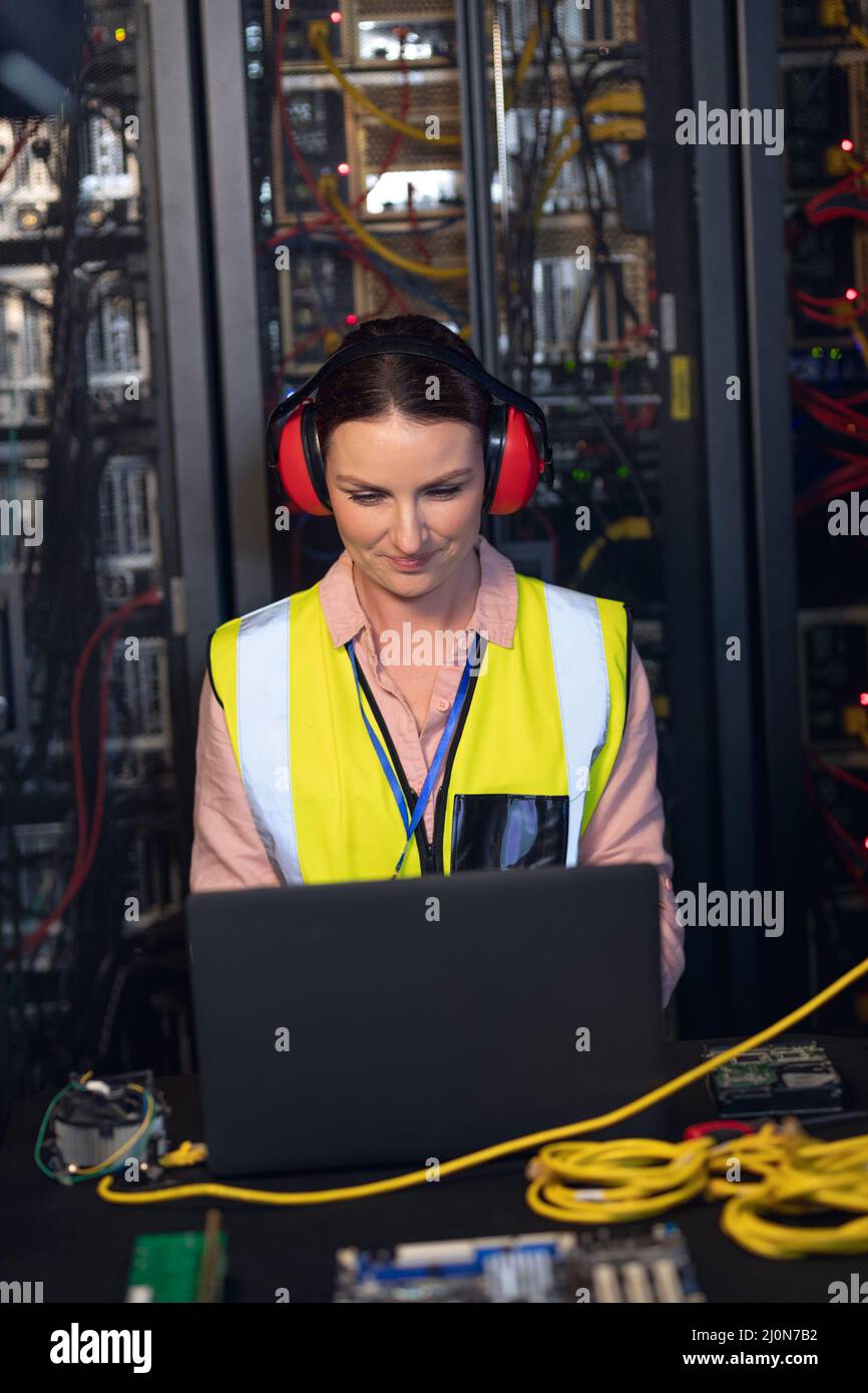 Caucasian female engineer wearing ear plugs using a laptop in computer ...