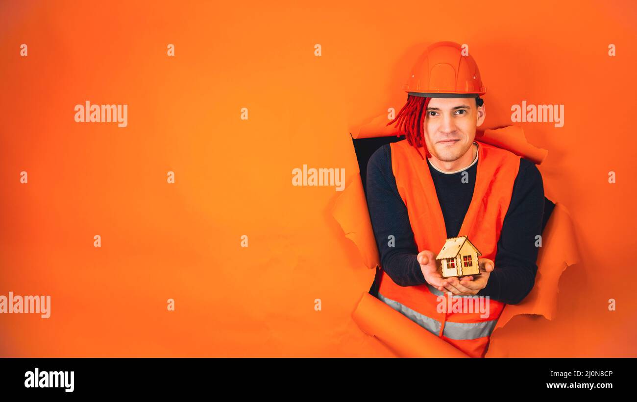 Male construction worker in overalls holding small wooden house and ...