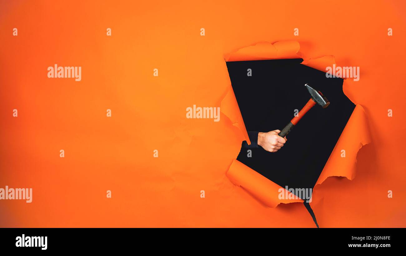 Man's hand with hammer sticking out of hole of orange background ...