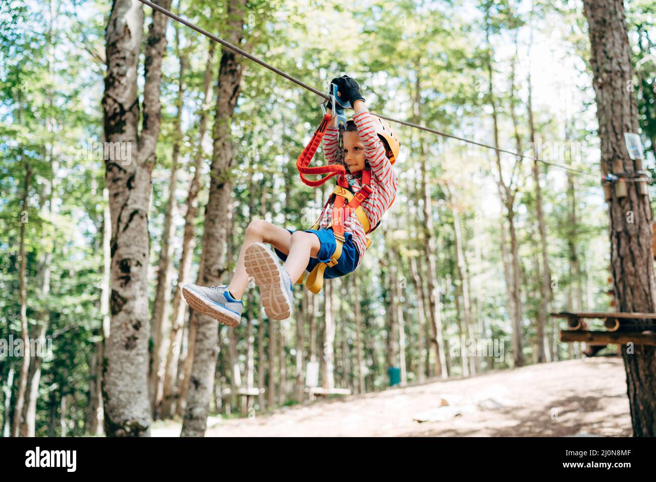 Boy goes down the zip line in the adventure park Stock Photo - Alamy