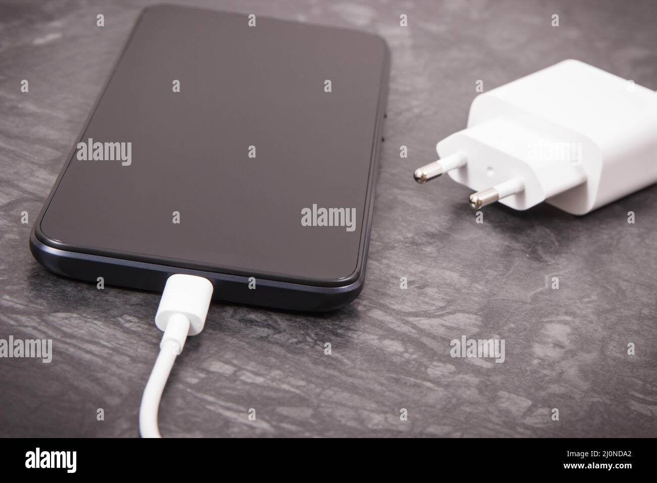 Black smartphone with connected white plug of charger. Telephone ...