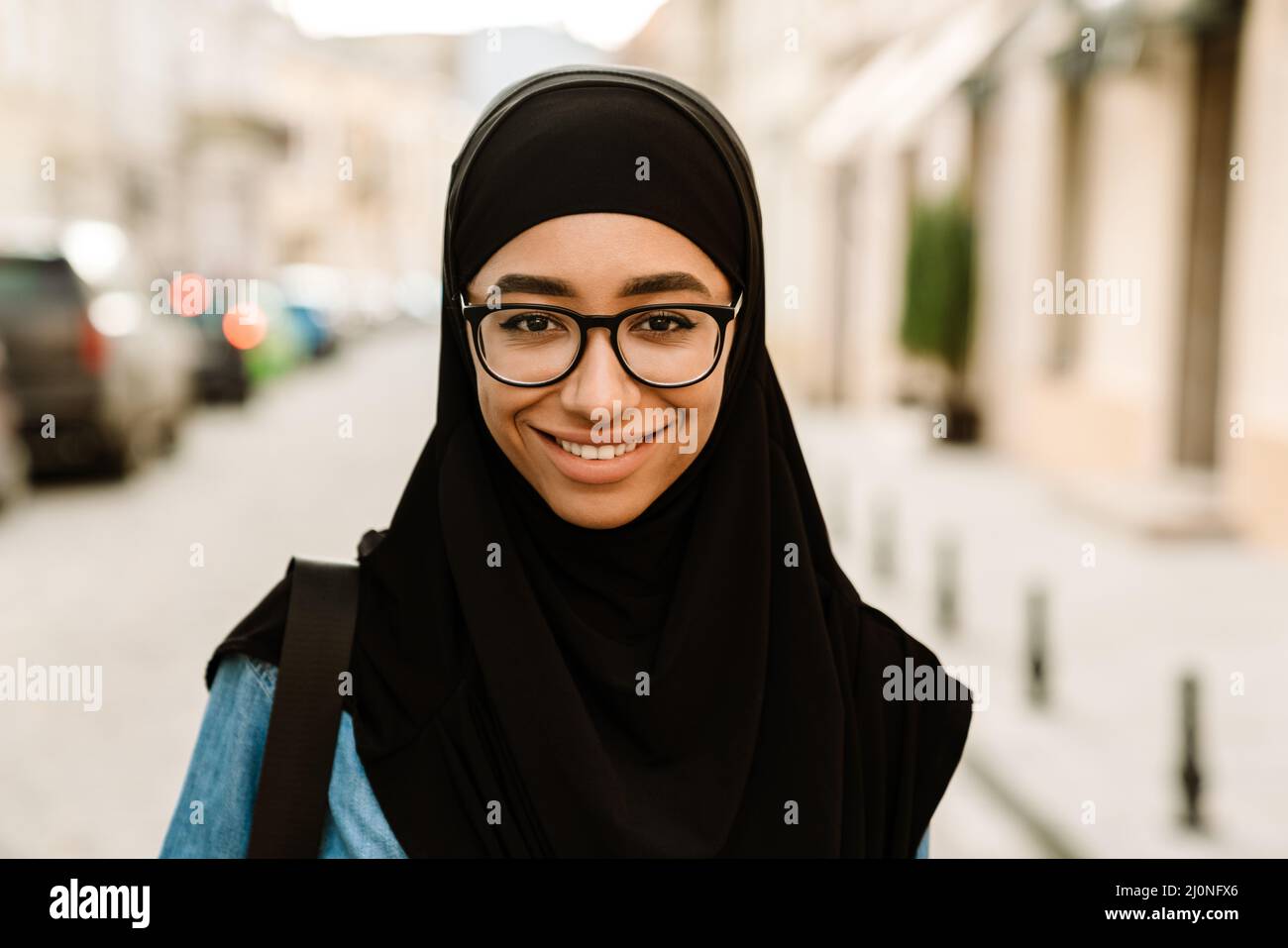 Close up of a smiling young muslim woman in hijab standing on a street ...