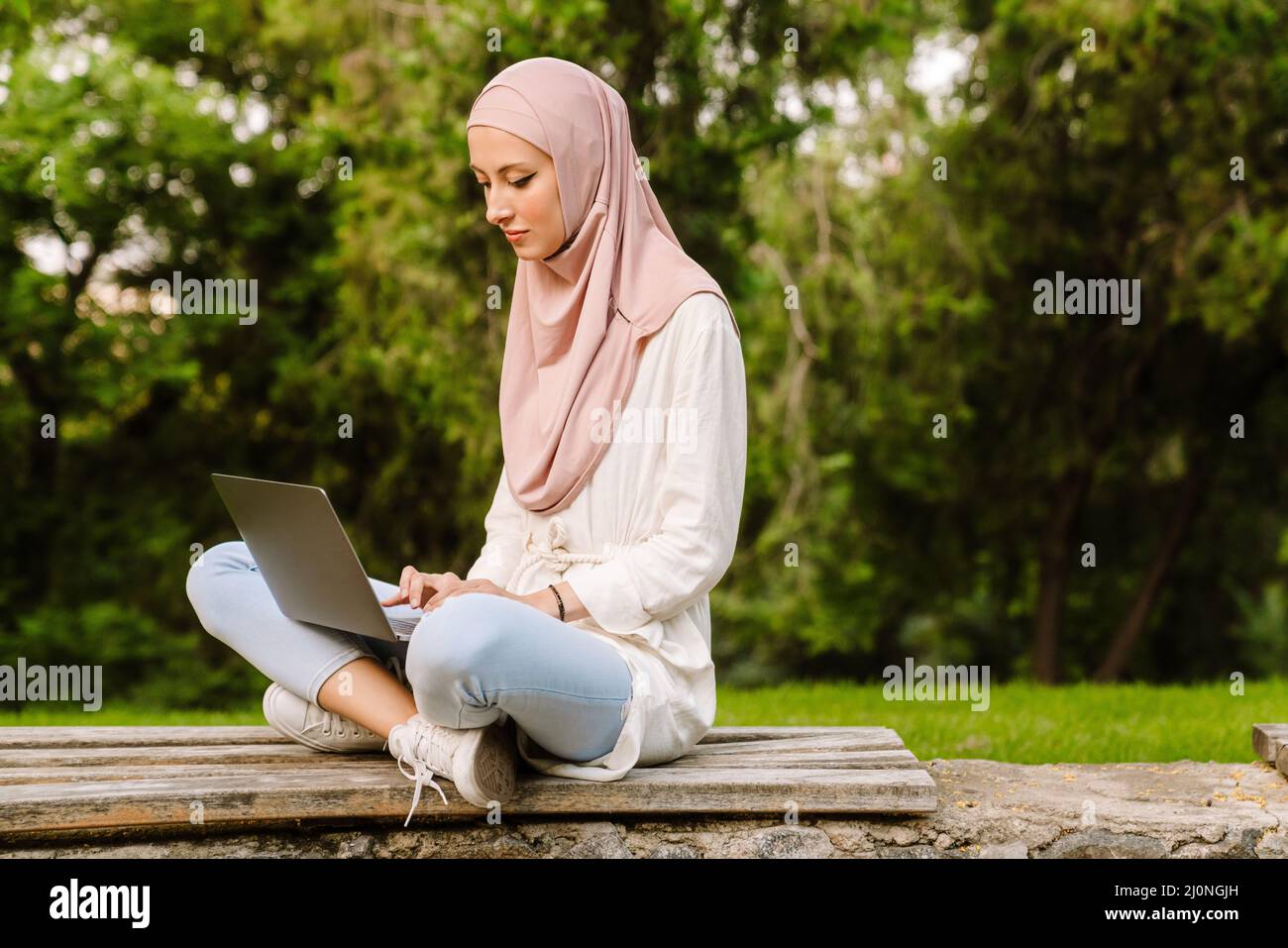 Smiling middle aged muslim woman sitting on a bench outdoors using ...