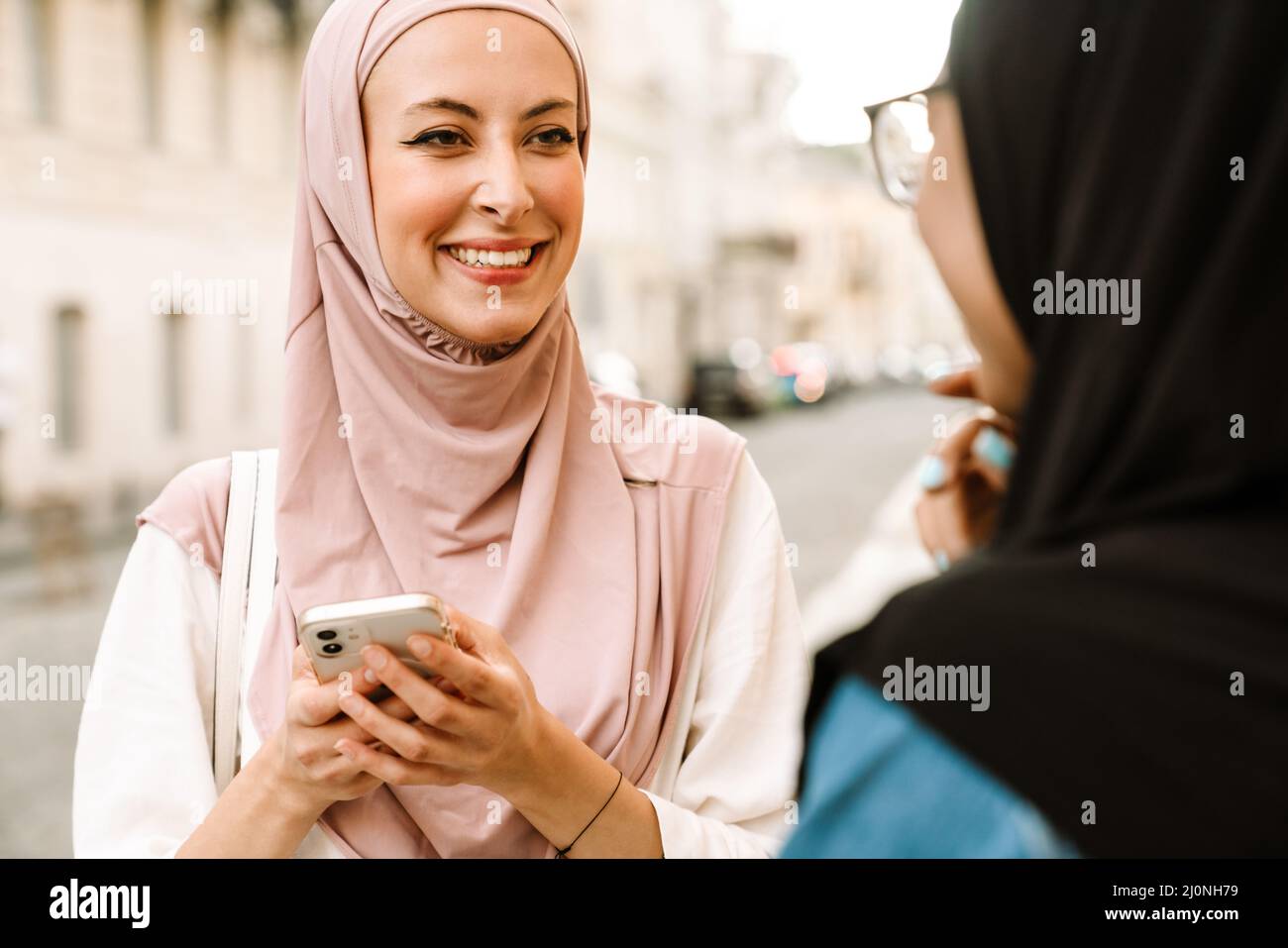 Multiracial muslim women wearing hijab talking while using mobile phone ...
