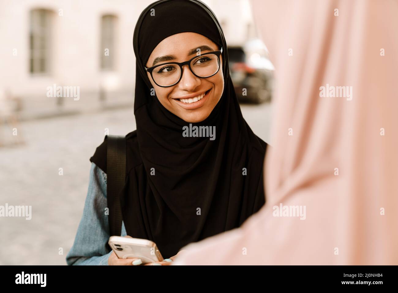 Two smiling young muslim women standing talking on a street close up ...